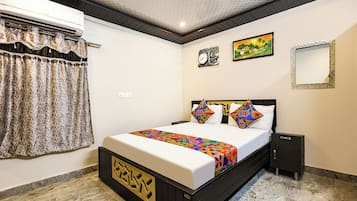 Quarto de hotel com cama, mesa de cabeceira, relógio de parede, quadro e espelho.