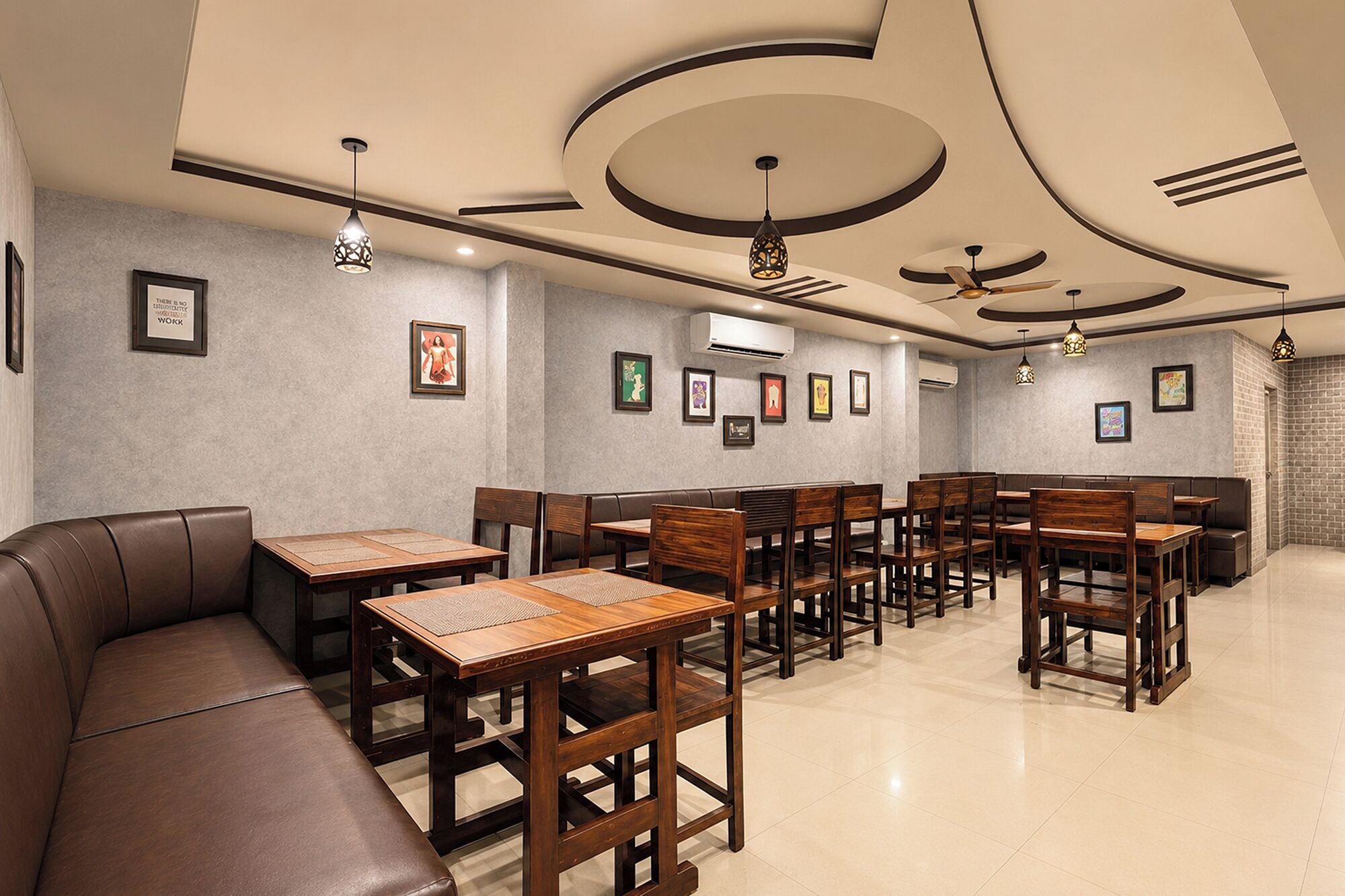 Interior de restaurante com mesas e cadeiras de madeira, um assento em couro e quadros nas paredes.