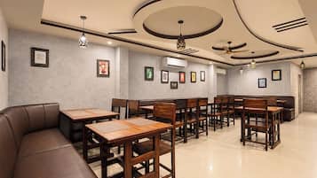 Interior de restaurante com mesas e cadeiras de madeira, um assento em couro e quadros nas paredes.