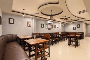 Interior de restaurante com mesas e cadeiras de madeira, um assento em couro e quadros nas paredes.
