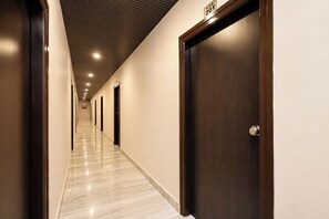 Corredor de hotel com portas, piso de mármore e iluminação embutida no teto.