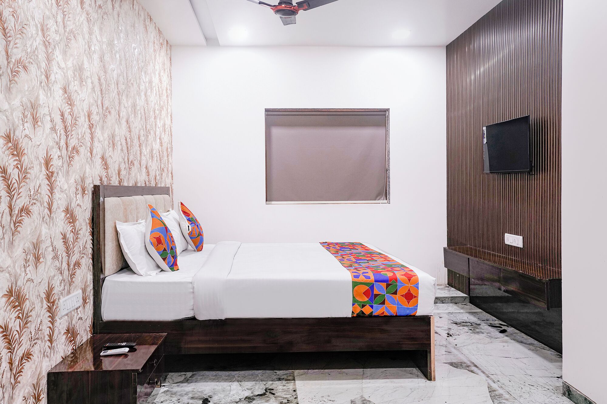 Quarto com cama, televisão na parede e janela com persiana.