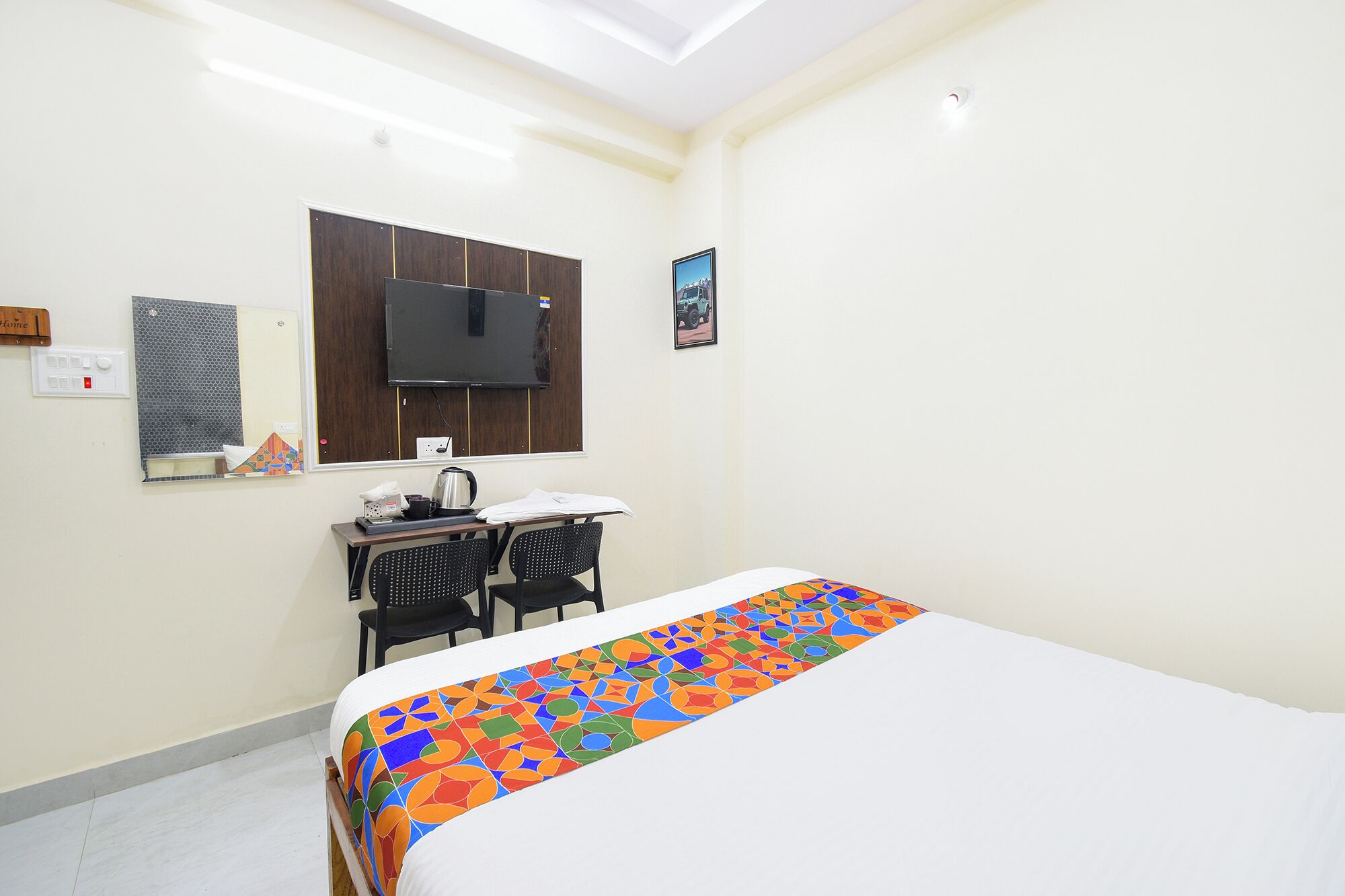 Quarto de hotel com uma cama, uma mesa com cadeira, uma televisão na parede e um pequeno porta-retrato.