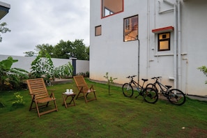 Um pátio com duas cadeiras de madeira, uma mesa, uma bicicleta e um edifício branco com janelas e uma porta.