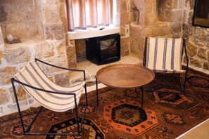 Quarto com paredes de pedra, duas cadeiras, uma mesa redonda e um tapete estampado.
