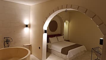 Quarto com uma grande porta em arco, cama com roupa de cama branca, banheira de madeira e uma bicicleta.