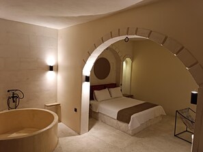 Quarto com uma grande porta em arco, cama com roupa de cama branca, banheira de madeira e uma bicicleta.
