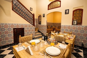 Uma sala de jantar com piso xadrez, uma escadaria com grades ornamentadas e um aposento com paredes estampadas.