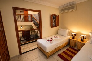 Quarto com cama, mesa de cabeceira, luminária, janela e porta que dá para uma escada.