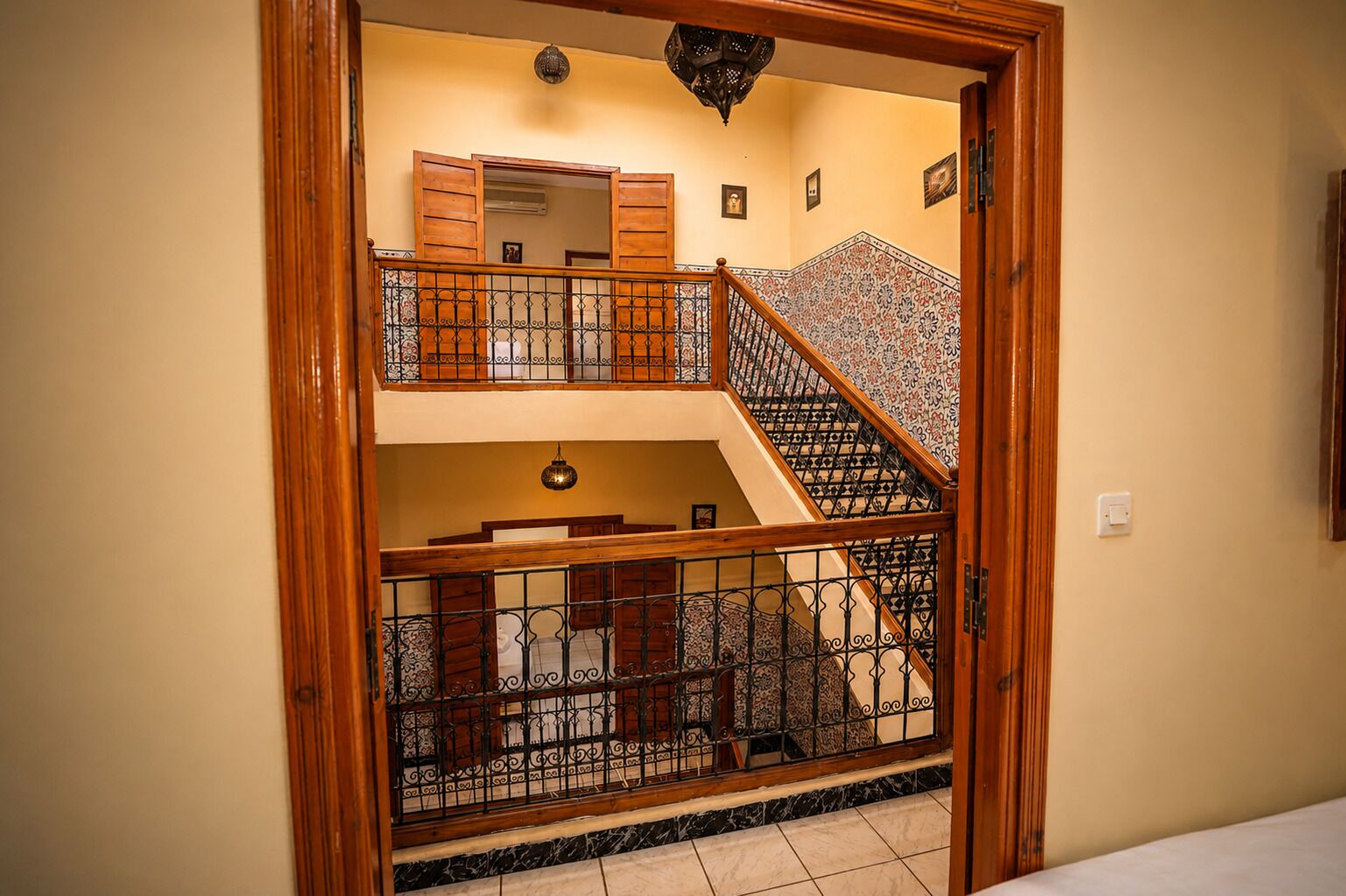 Um interior em vários níveis, com escadaria de madeira, guarda-corpos de metal e paredes com padrão.