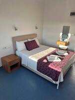 Uma cama de solteiro com cabeceira, mesa de cabeceira, espelho e tomada na parede.