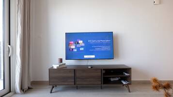 Uma sala de estar moderna com uma televisão de tela plana fixada em um armário de madeira, uma janela com cortinas e uma pequena planta no chão.