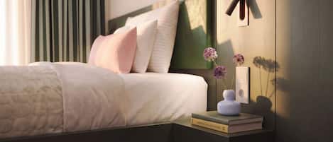 Cama bem arrumada com travesseiros, mesa de cabeceira com um livro e um vaso de flores, e um interruptor de luz fixado na parede.