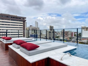 Uma área de piscina no terraço com espreguiçadeiras e vista para o horizonte da cidade.