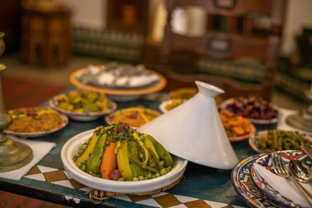 Mesa de jantar com diversos pratos, incluindo um prato de cuscuz com legumes e uma panela branca.