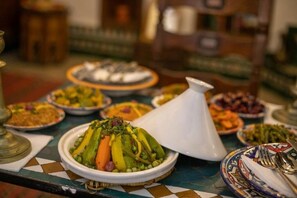 Mesa de jantar com diversos pratos, incluindo um prato de cuscuz com legumes e uma panela branca.