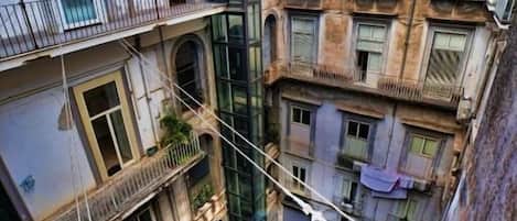 Uma rua estreita na cidade, com edifícios em ambos os lados, um carro estacionado e uma bicicleta.