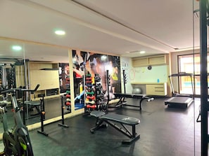 Uma academia com equipamentos de ginástica, um banco e esteira.