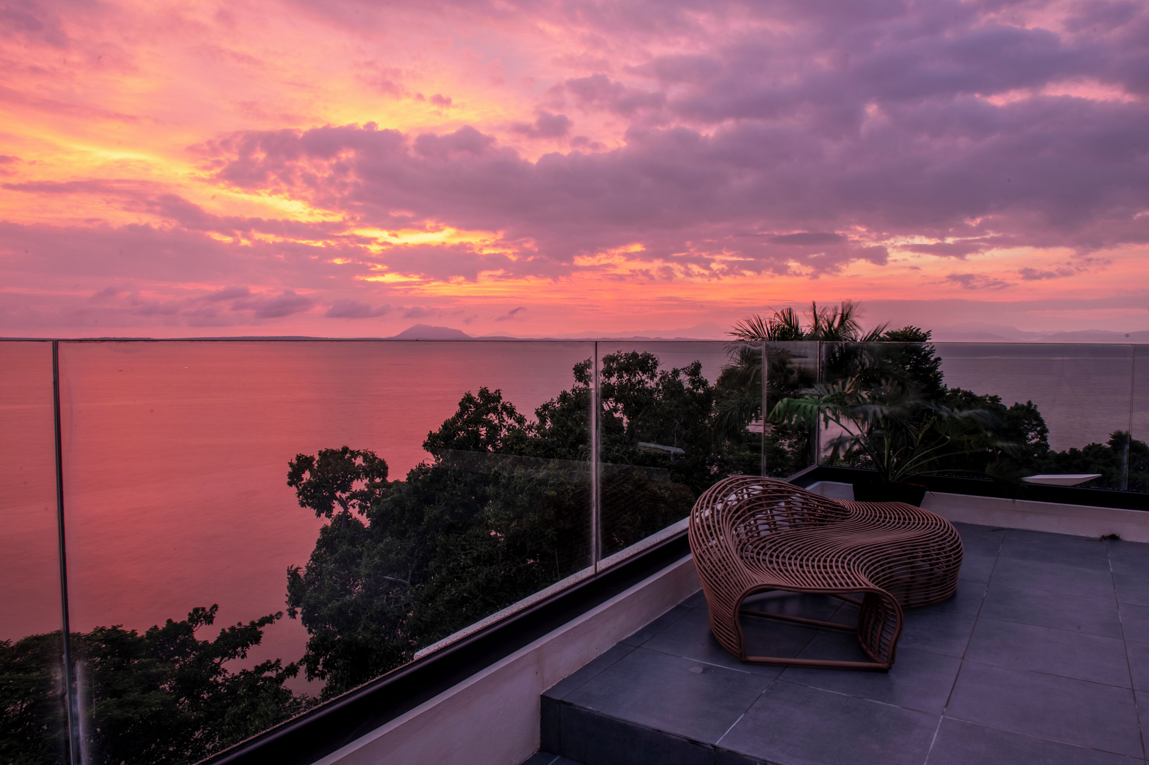 Varanda com cadeira de vime com vista para a água e um pôr do sol.