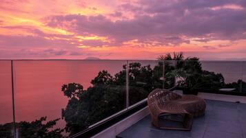 Varanda com cadeira de vime com vista para a água e um pôr do sol.