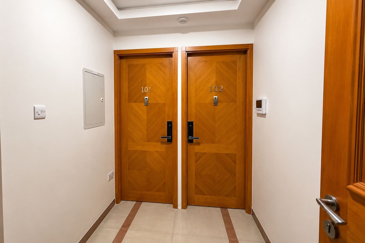 Corredor com duas portas de madeira com as etiquetas 101 e 102, um interruptor de luz e um termostato na parede.