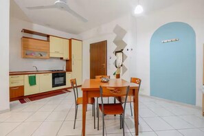 Uma sala de jantar com uma mesa e cadeiras de madeira, uma cozinha com armários de madeira e uma porta azul.