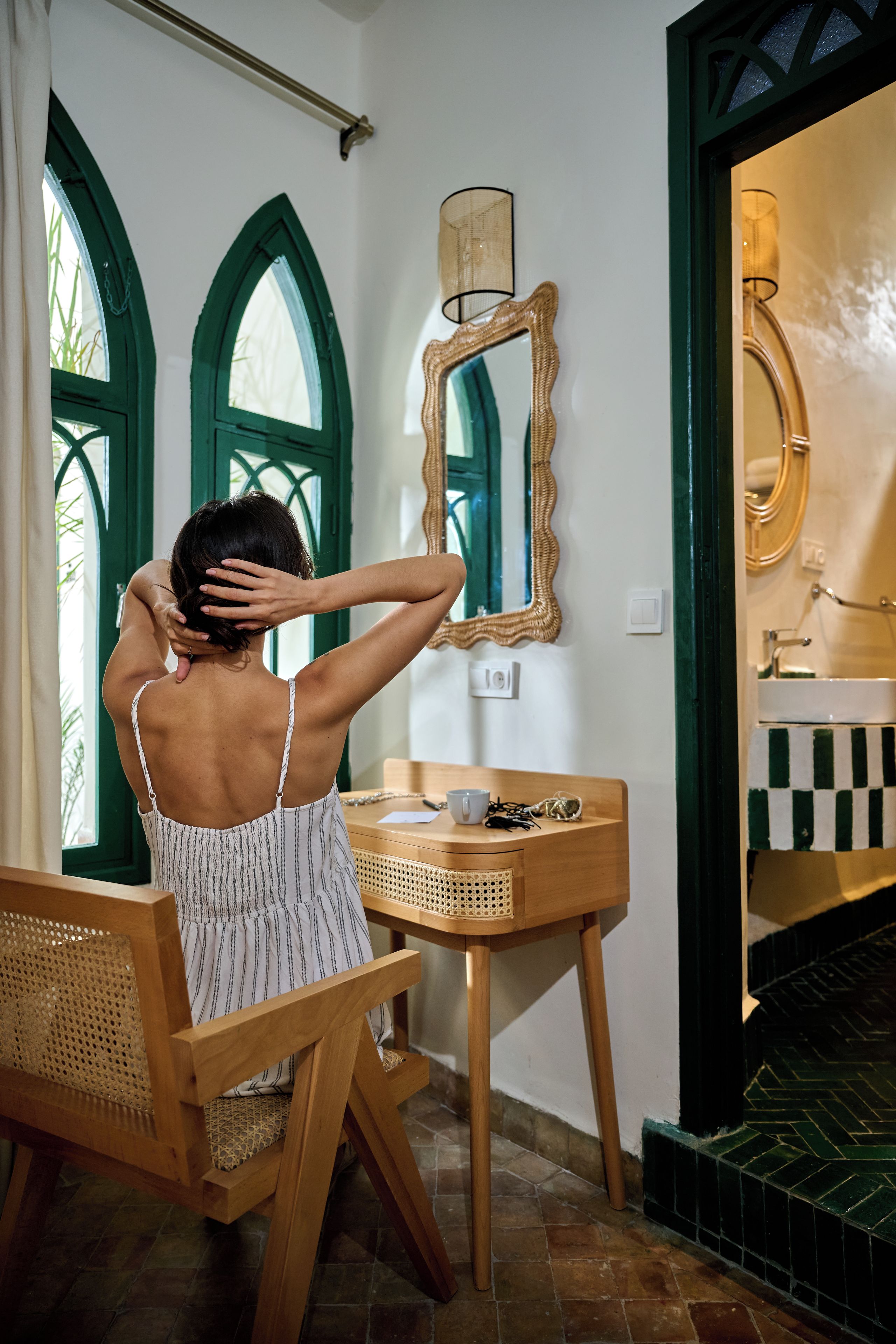 Quarto com escrivaninha de madeira, espelho e janela com moldura verde.