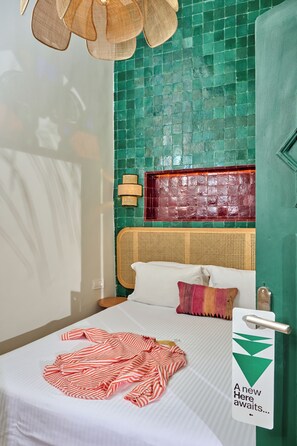 Quarto de hotel com cama, parede revestida de azulejos verdes, cabeceira de tecido e uma placa na porta.