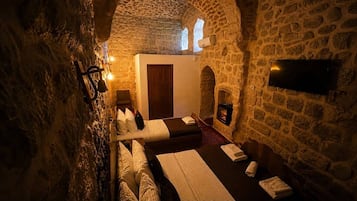Quarto com paredes de pedra, uma cama, uma porta de madeira, uma televisão de tela plana e uma lareira.