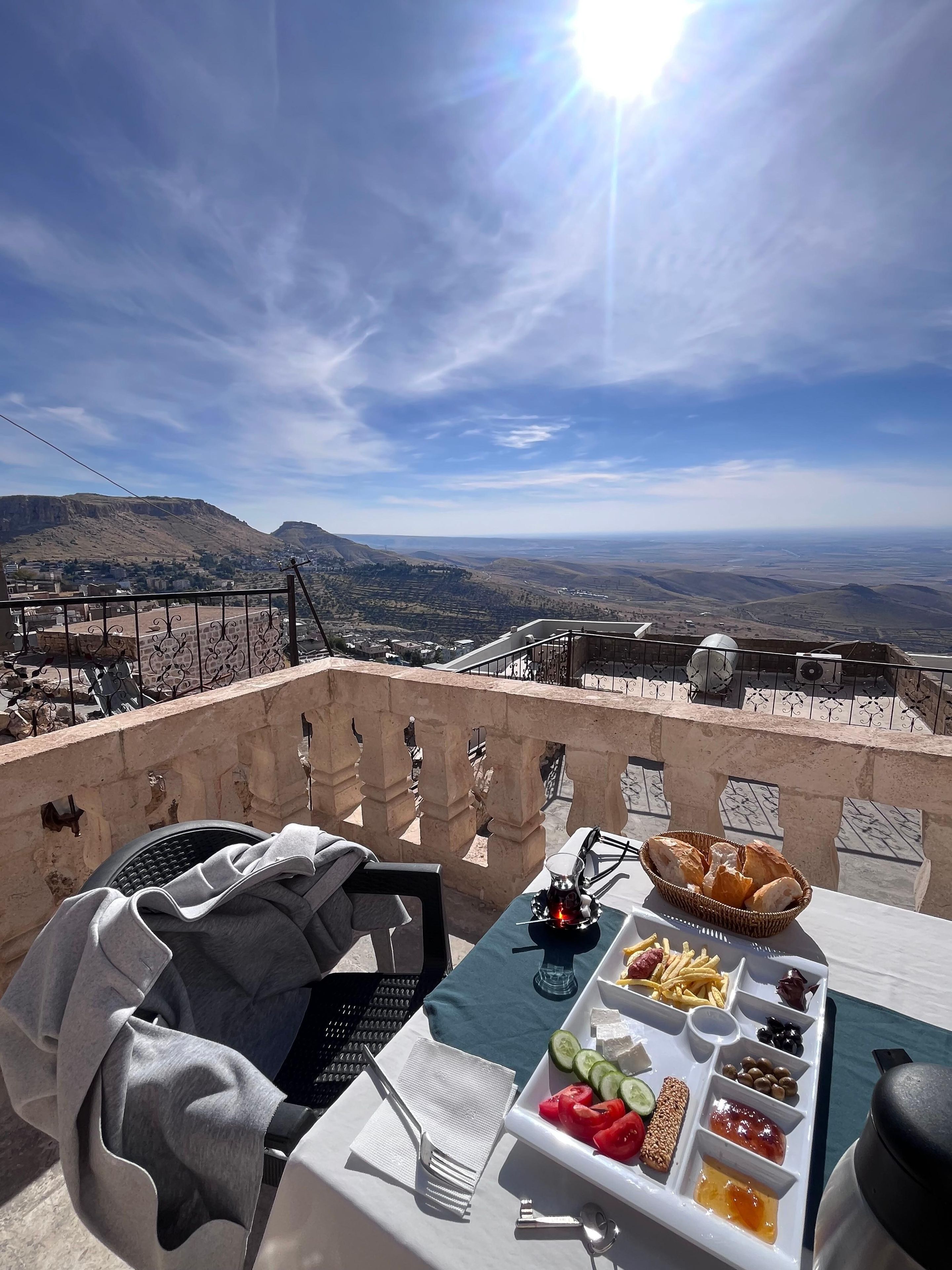 Mesa com refeição em varanda com vista para paisagem montanhosa.