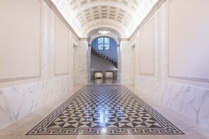 Um corredor com piso de mármore e um padrão geométrico que leva a uma escadaria.