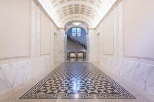 Um corredor com piso de mármore e um padrão geométrico que leva a uma escadaria.