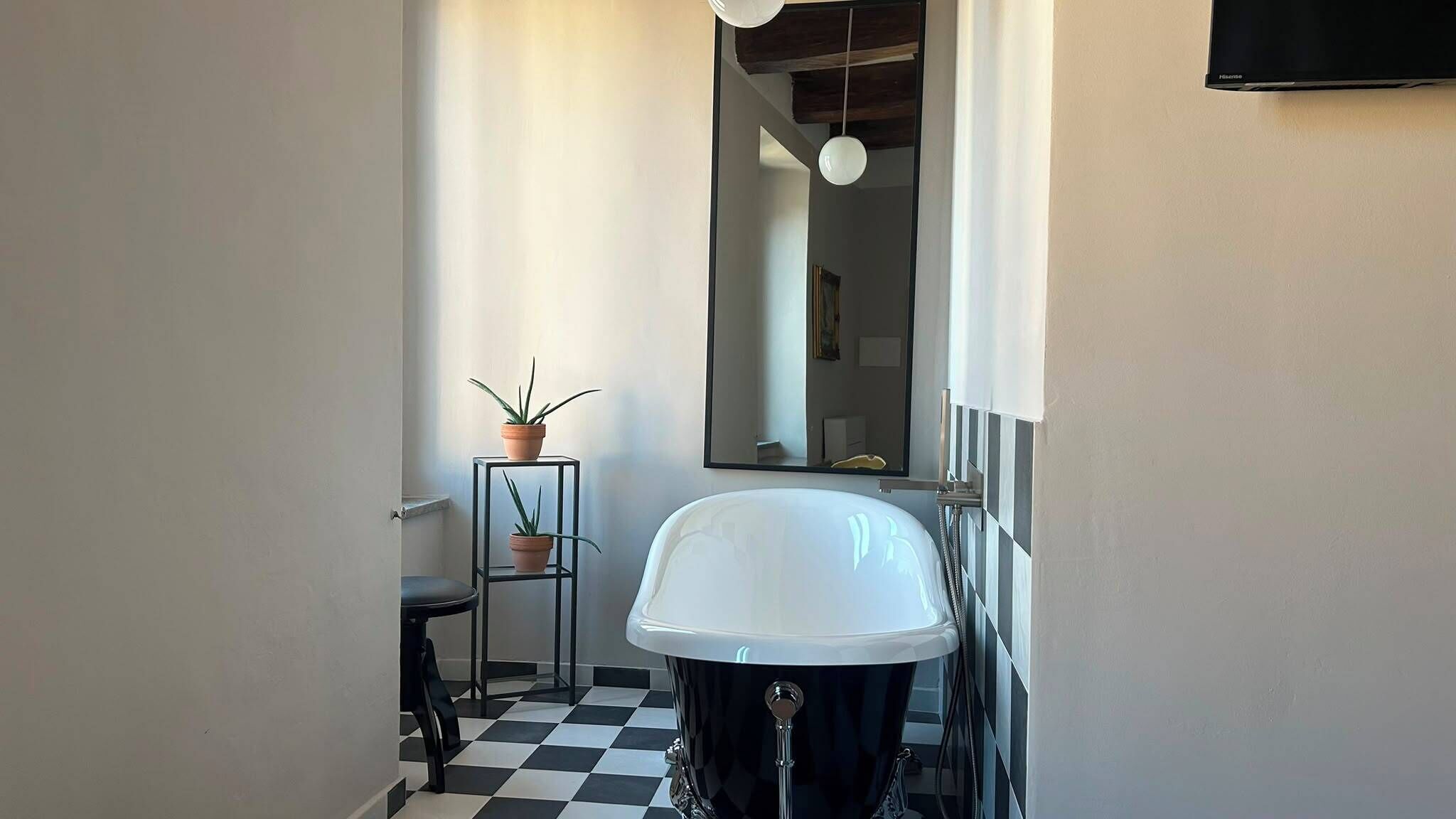 Casa de banho com lavatório branco, espelho e planta num suporte de metal.