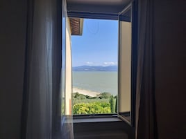 Quarto com uma grande janela com vista para a água e uma linha costeira distante.