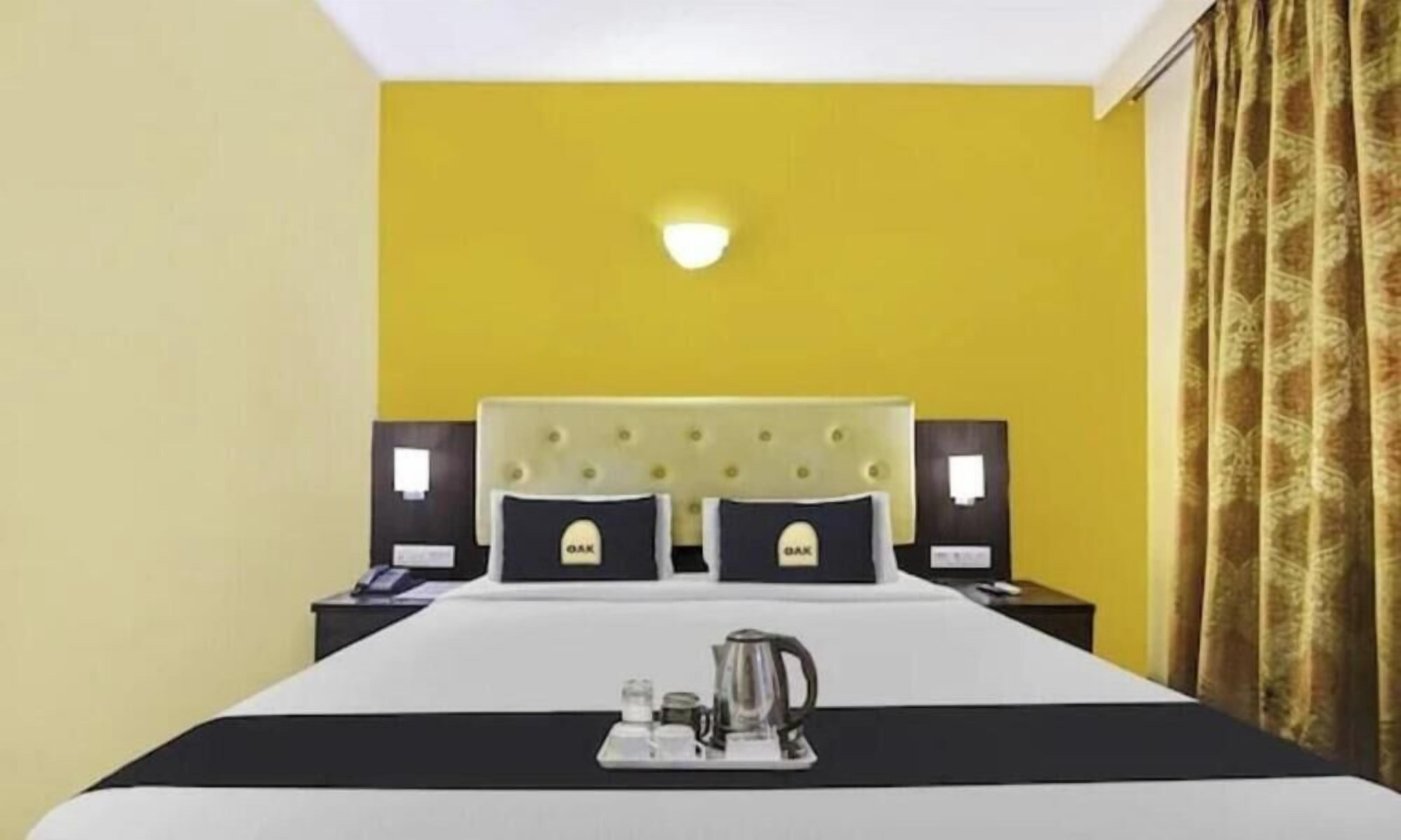 Quarto de hotel com cama, mesas de cabeceira, luminária na parede e cortina.