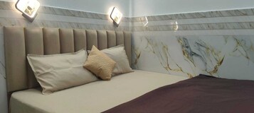 Quarto de hotel com cama, cabeceira e parede com padrão marmorizado.