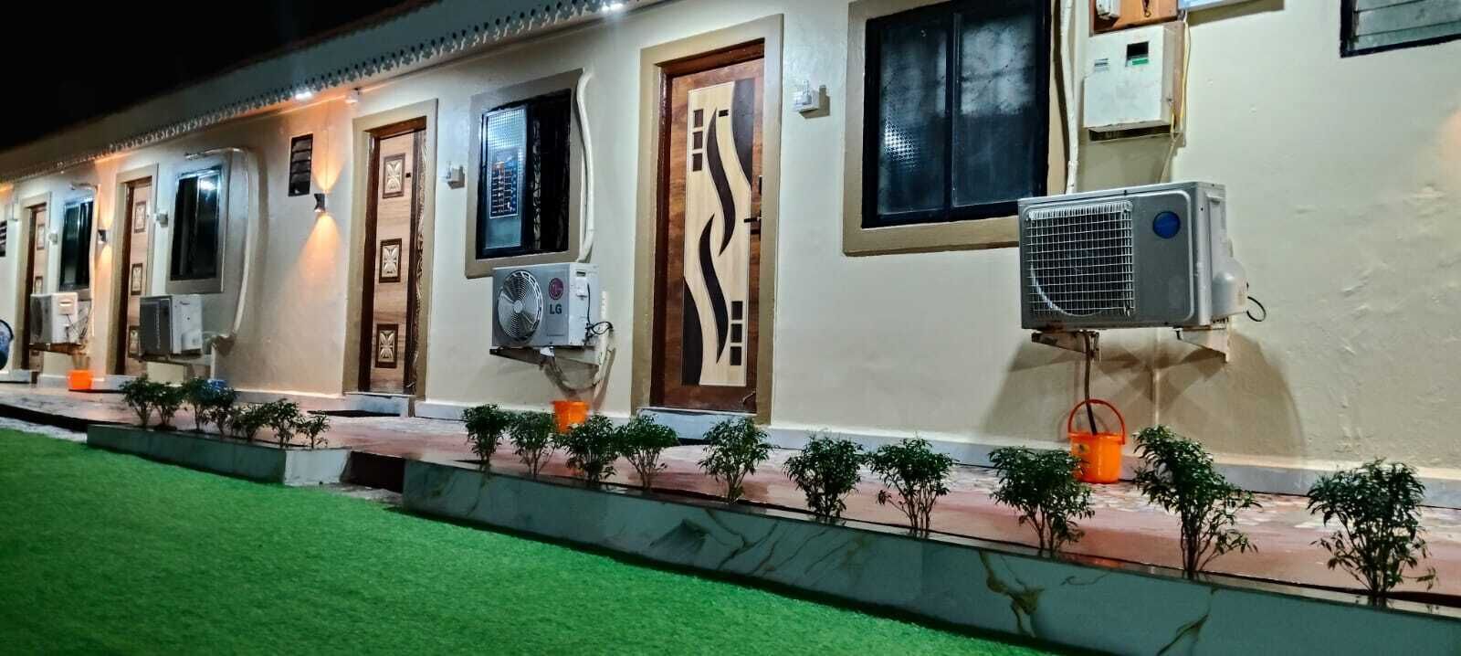 Vários quartos com aparelhos de ar condicionado, porta com padrão decorativo e pequenas plantas ao longo do caminho.
