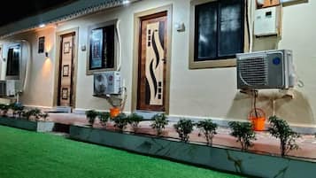 Vários quartos com aparelhos de ar condicionado, porta com padrão decorativo e pequenas plantas ao longo do caminho.