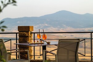 Uma mesa com um pilar de pedra, dois copos de bebida, uma pequena travessa e uma tigela, com montanhas ao fundo.