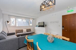 Uma sala de estar moderna com um sofá, uma mesa de jantar com cadeiras, uma televisão e uma porta com a inscrição 'SALIDA'.
