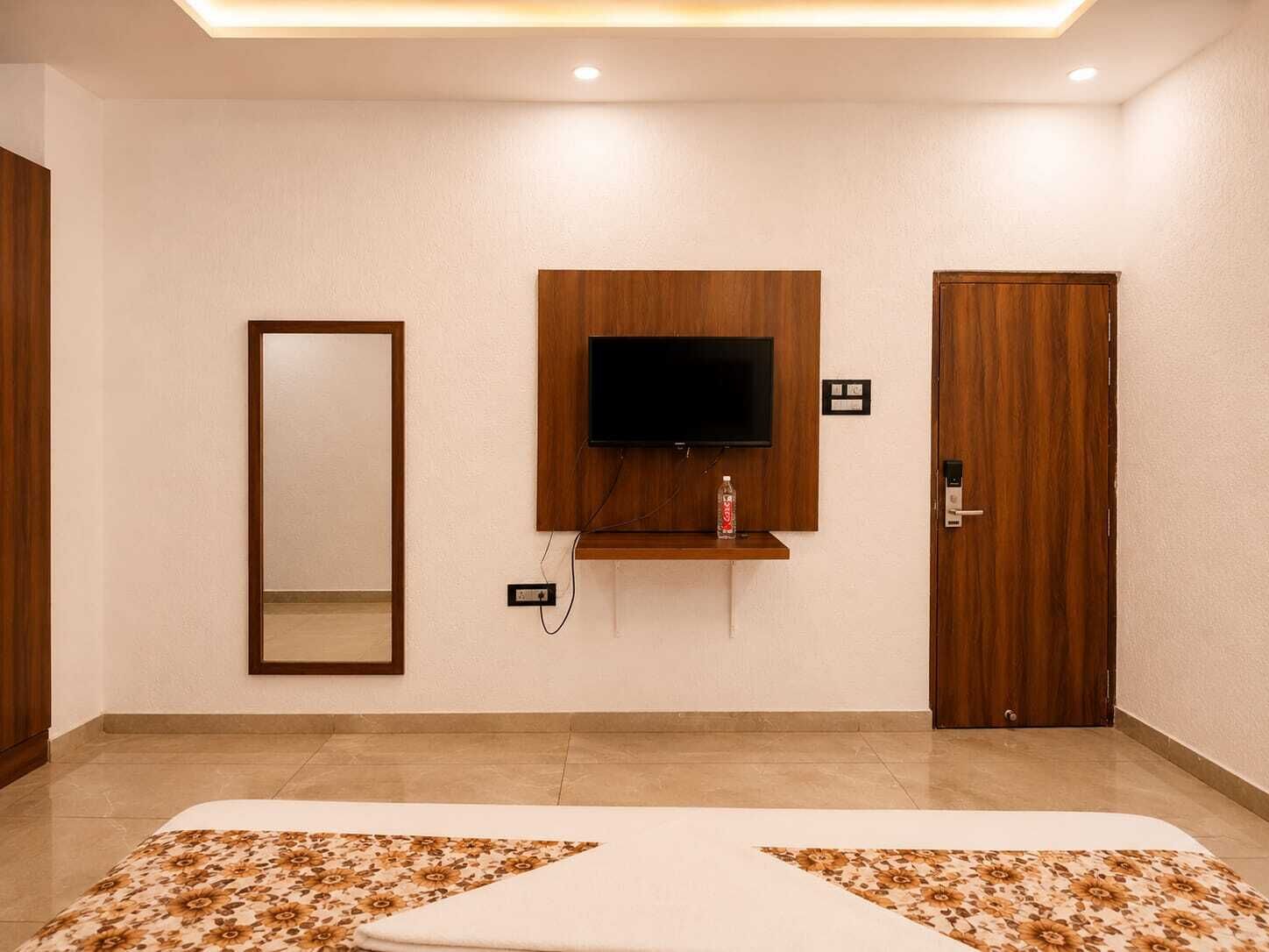 Quarto de hotel com cama, televisão na parede, porta e espelho.
