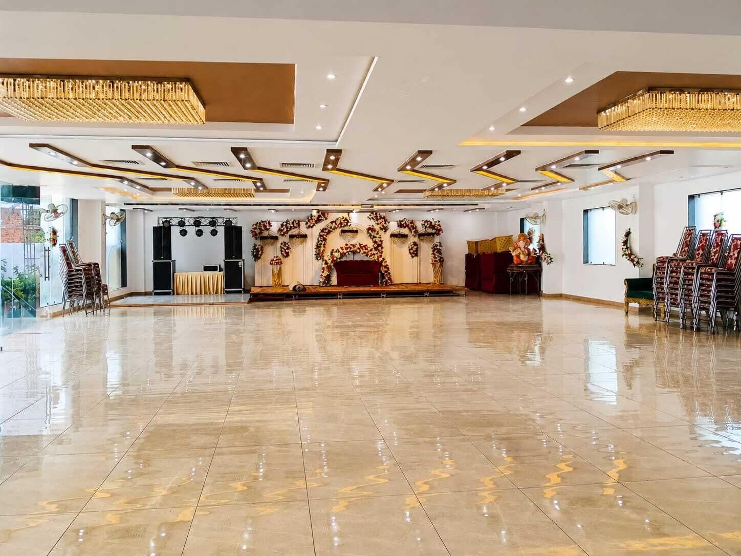 Um salão amplo com piso lustroso, um palco com decorações florais e uma área de estar com cadeiras.