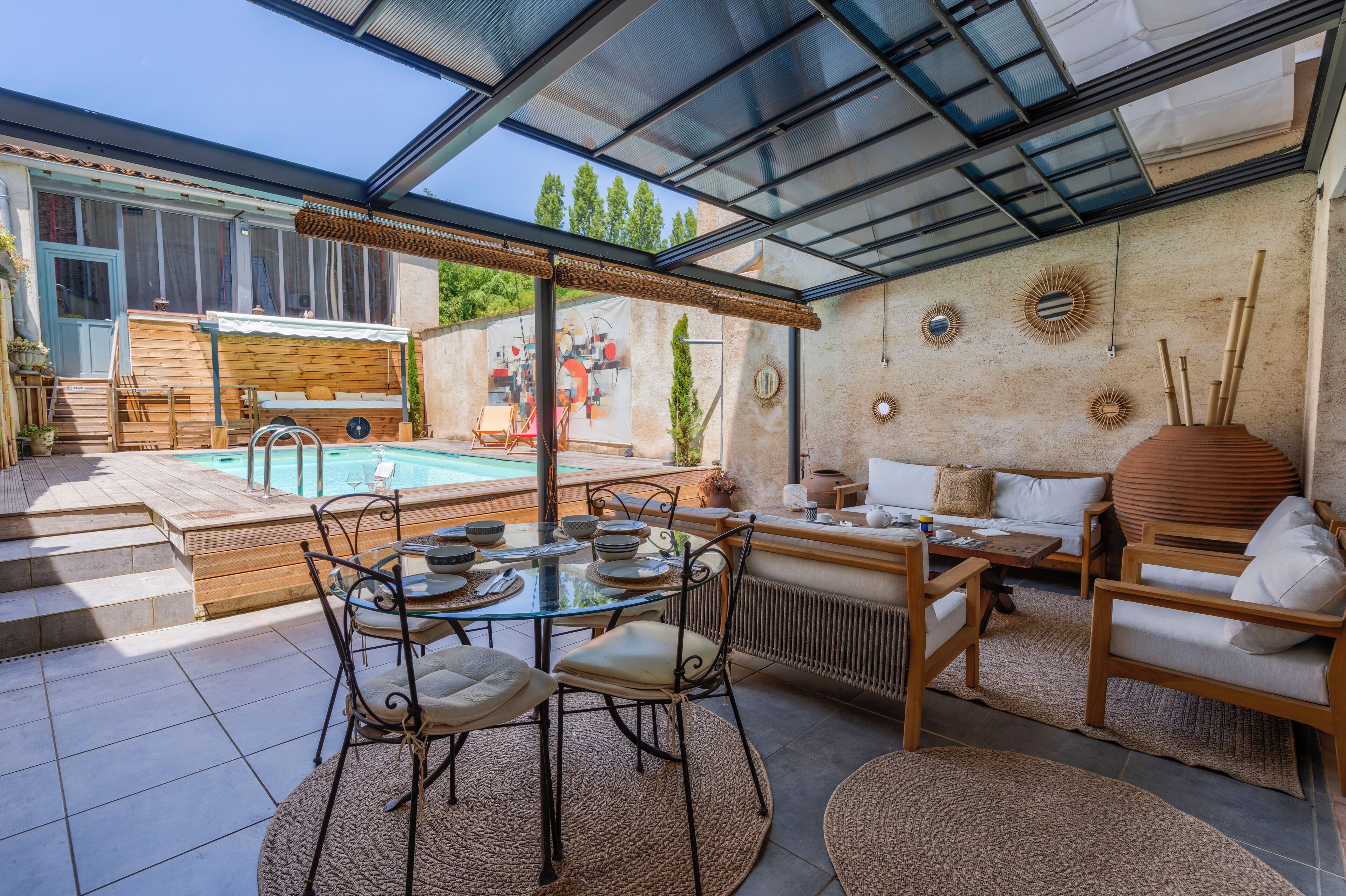 Pátio ao ar livre ensolarado com piscina, área de jantar e espaço para sentar.