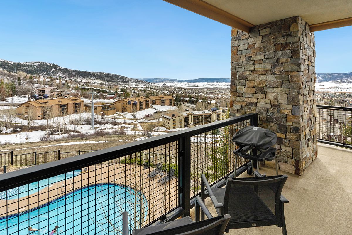 Uma varanda com um pilar de pedra, piscina e vista para uma área residencial com colinas cobertas de neve.