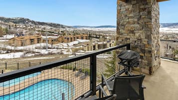 Uma varanda com um pilar de pedra, piscina e vista para uma área residencial com colinas cobertas de neve.