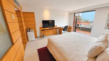 Quarto de hotel com cama, escrivaninha, televisão e vista da cidade por uma grande janela.