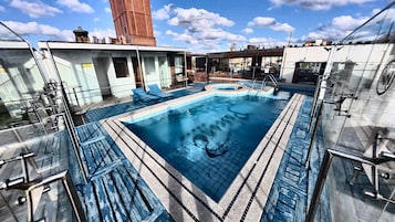 Piscina no terraço com spa, espreguiçadeiras e vista para o horizonte da cidade.