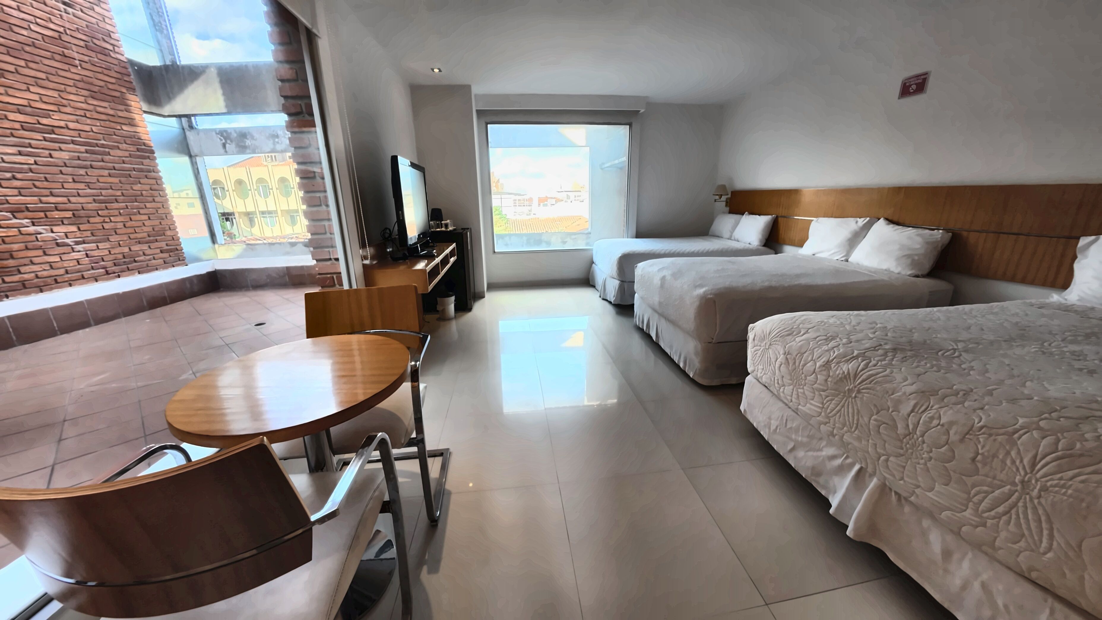 Quarto de hotel com varanda, mesa de jantar e duas camas.