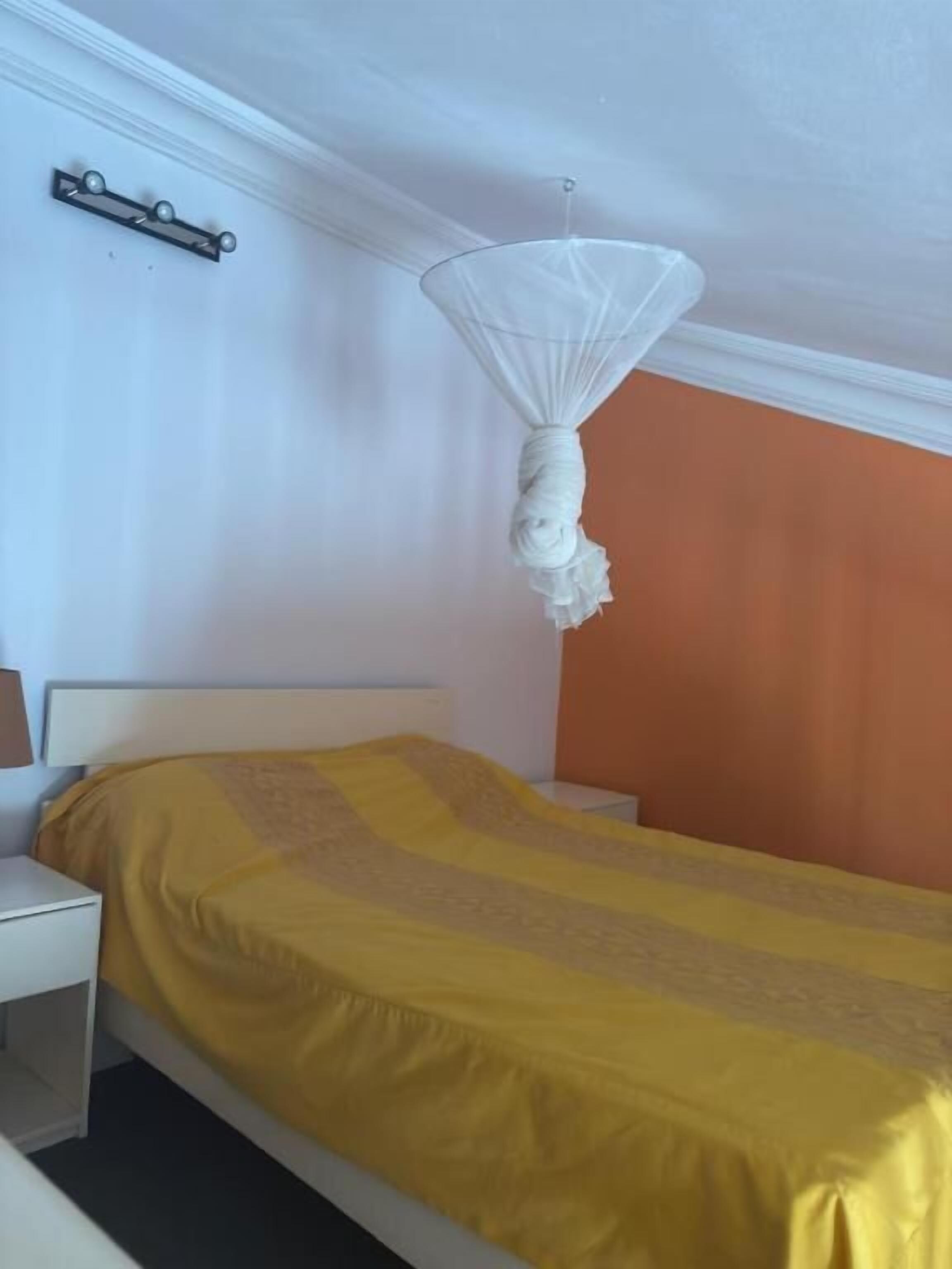 Uma cama com um edredom amarelo, uma mesa de cabeceira branca e uma mosquiteira pendurada.