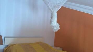 Uma cama com um edredom amarelo, uma mesa de cabeceira branca e uma mosquiteira pendurada.